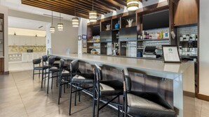 Uma área de bar moderna, com um balcão extenso, banquetas e diversas garrafas e copos.