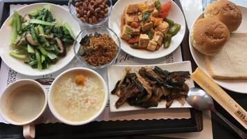 Uma bandeja com diversos pratos, incluindo tofu, legumes e sopa, juntamente com duas chávenas e pães.