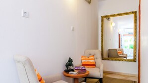 Um quarto com duas poltronas, uma mesinha com livros e uma estátua, e um espelho grande na parede.