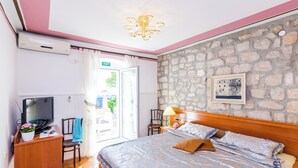 Quarto com cama, televisão, escrivaninha com computador, cadeira e parede de pedra.