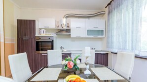 Cozinha moderna com armários brancos, forno embutido e área de jantar com mesa de vidro e cadeiras brancas.
