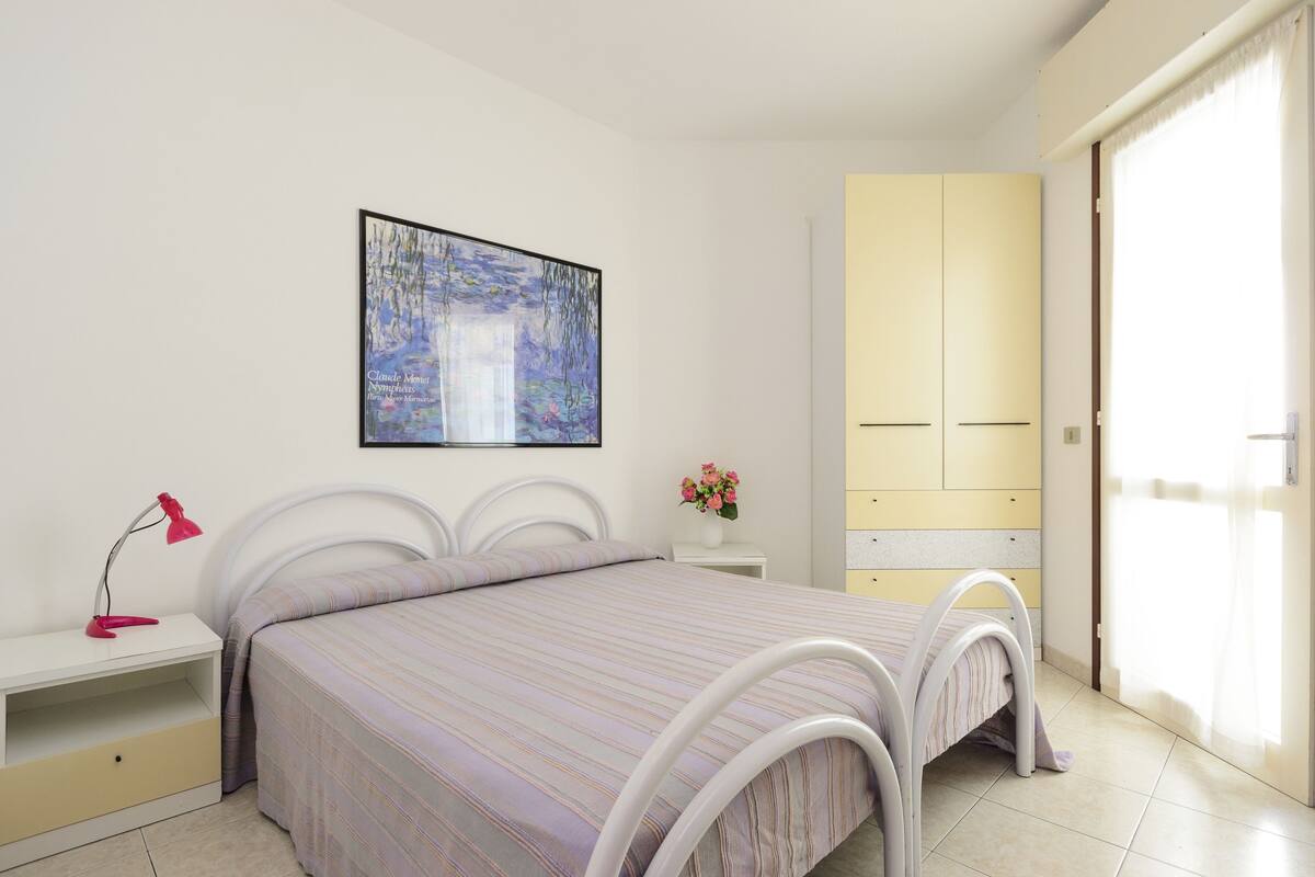 Quarto com cama, mesa de cabeceira, escrivaninha, cadeira, guarda-roupa e um quadro na parede.