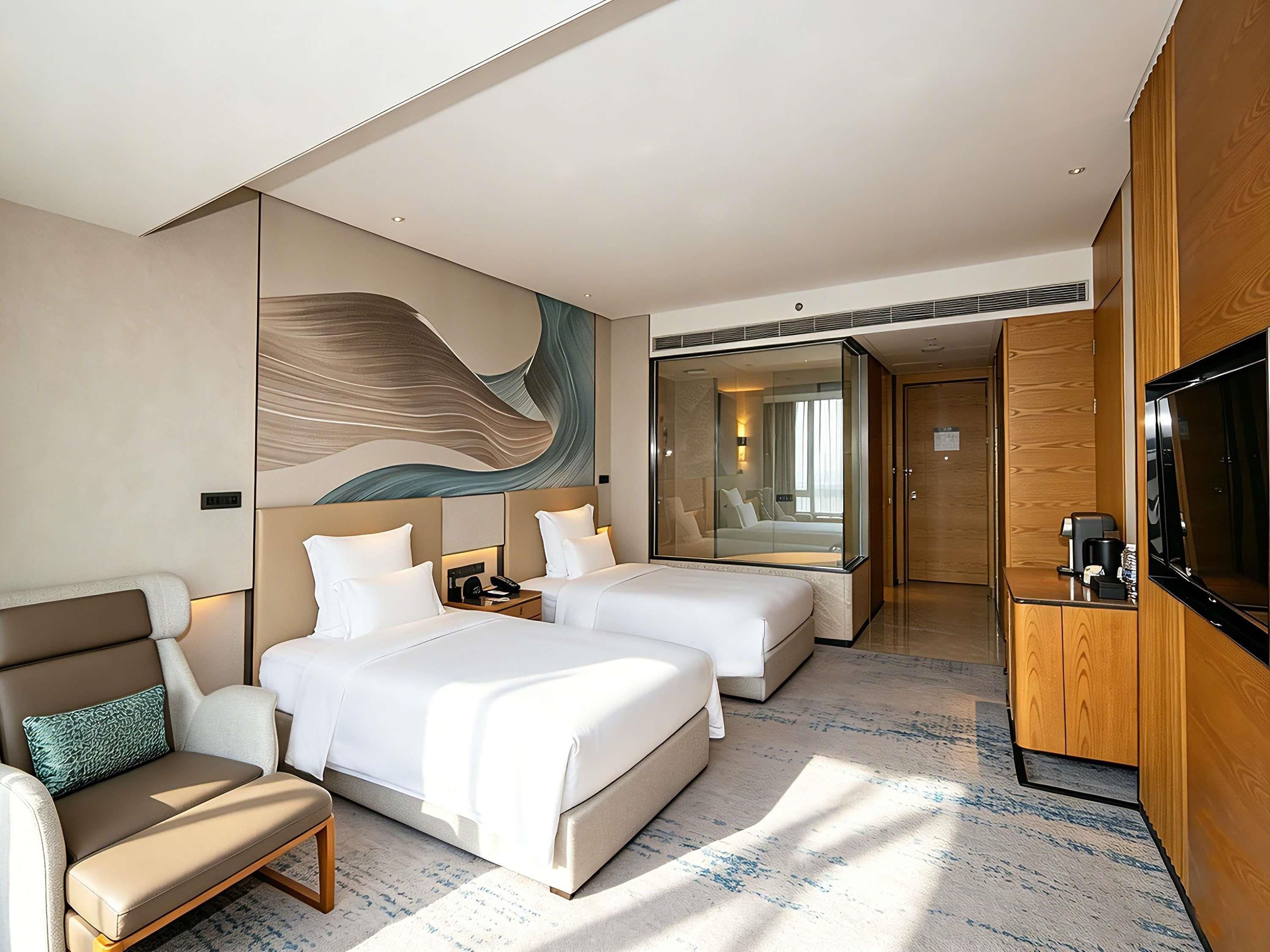 Quarto de hotel com duas camas, área de estar, televisão e um espelho grande.
