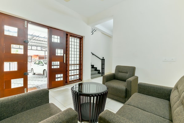 Uma sala de estar com uma mesa de centro de vidro, dois sofás cinza e uma porta de madeira que dá para o exterior.