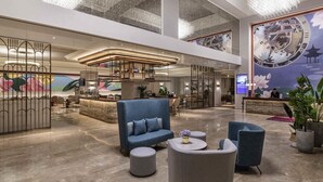 Um hall amplo com teto alto, área de bar, disposição de assentos e um grande painel decorativo.