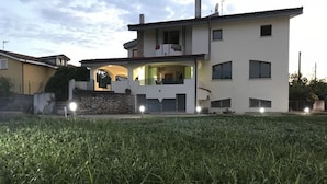 Uma casa de dois andares com varanda, muro de pedra e um jardim da frente bem iluminado.