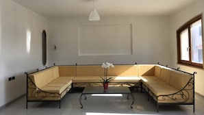 Uma sala de estar moderna com um sofá modular bege, uma mesa de centro de vidro e uma luminária pendente branca.
