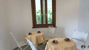 Um quarto com duas mesas redondas, cada uma com toalha amarela, e cadeiras de metal branco.