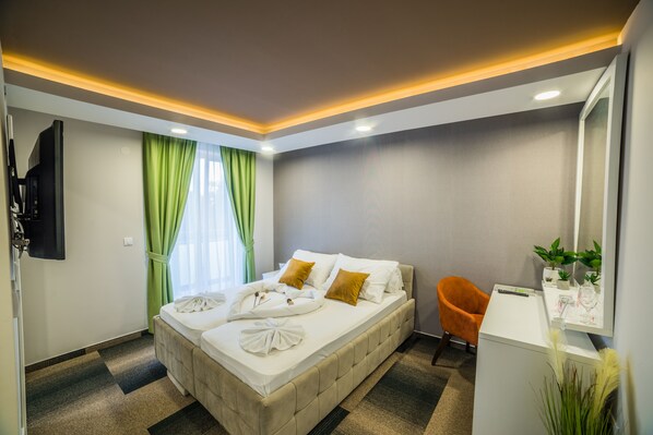 Quarto de hotel moderno com uma cama grande, uma escrivaninha, uma cadeira e uma televisão na parede.