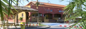 Uma área de recepção com um edifício vermelho, uma estrutura com telhado de palha e bicicletas estacionadas do lado de fora.