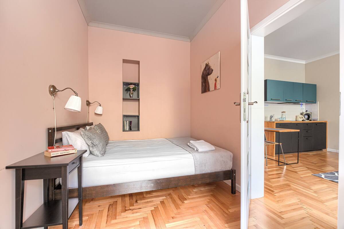 Quarto com cama, mesa de cabeceira, abajur e vista para a cozinha.