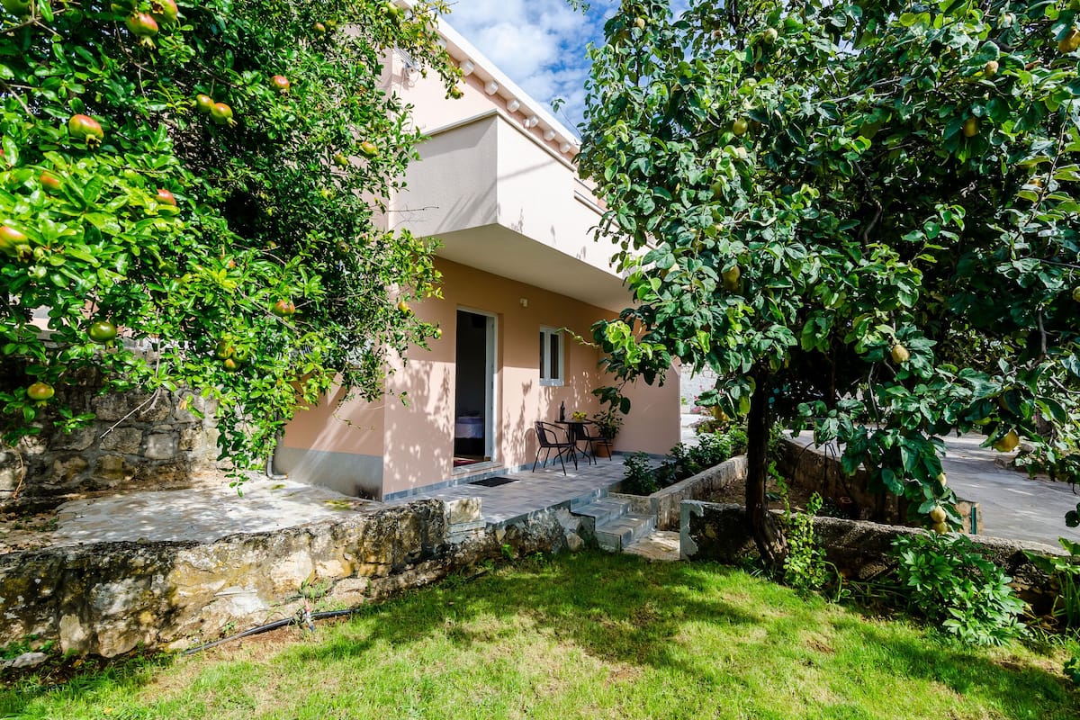 Um edifício com escadaria de pedra que leva a uma porta, cercado por vegetação exuberante e árvores frutíferas.