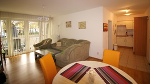 Sala de estar com sofá, mesa de jantar com cadeiras, cozinha ao fundo e varanda com vista.