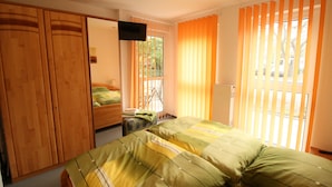 Quarto com cama, guarda-roupa, televisão e janela com cortinas.