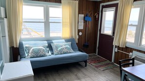 Quarto aconchegante com um sofá azul, paredes de madeira, vista para a praia e uma pequena mesa.