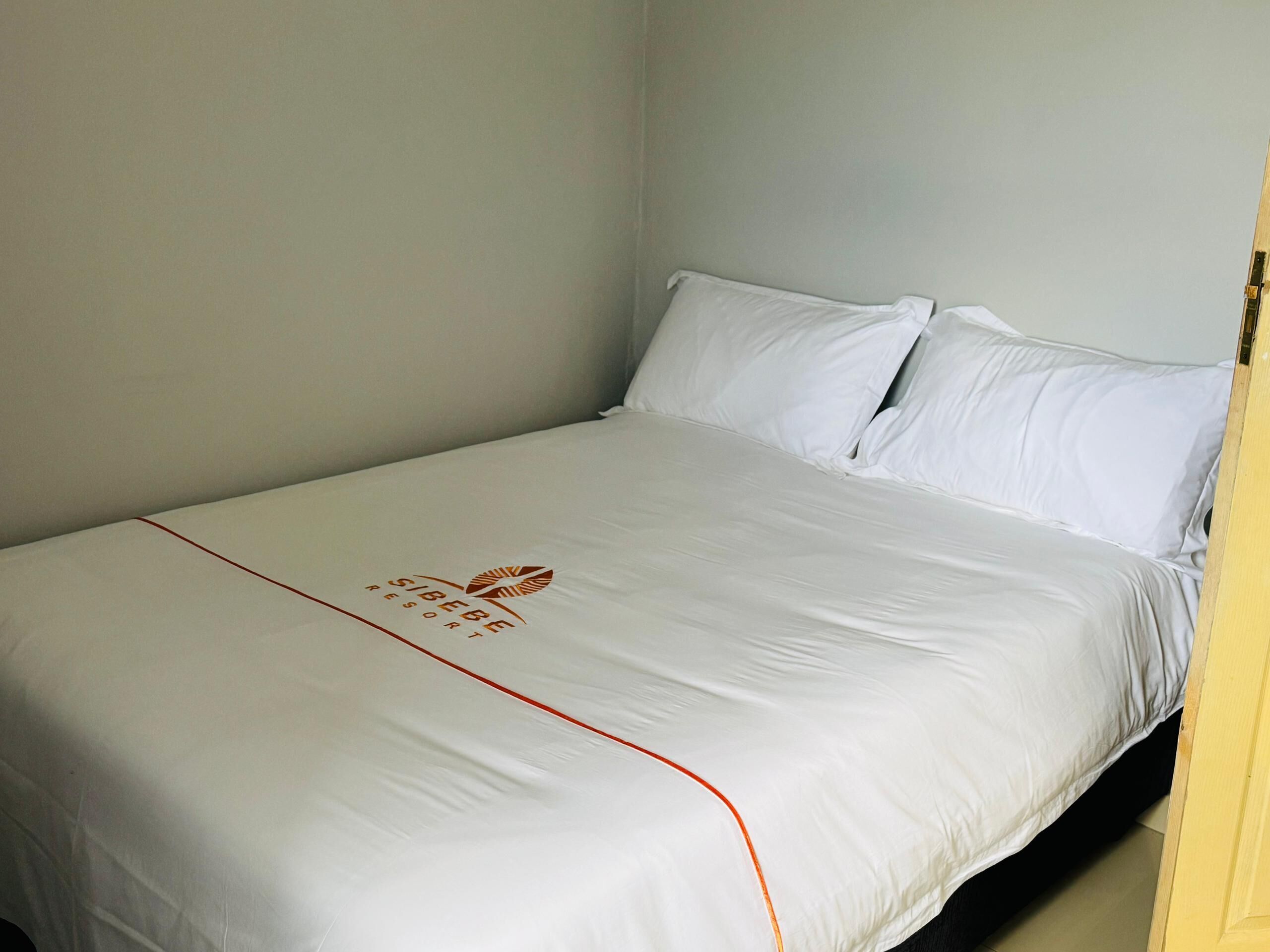 Uma cama de solteiro com roupa de cama branca e um logotipo na cabeceira.