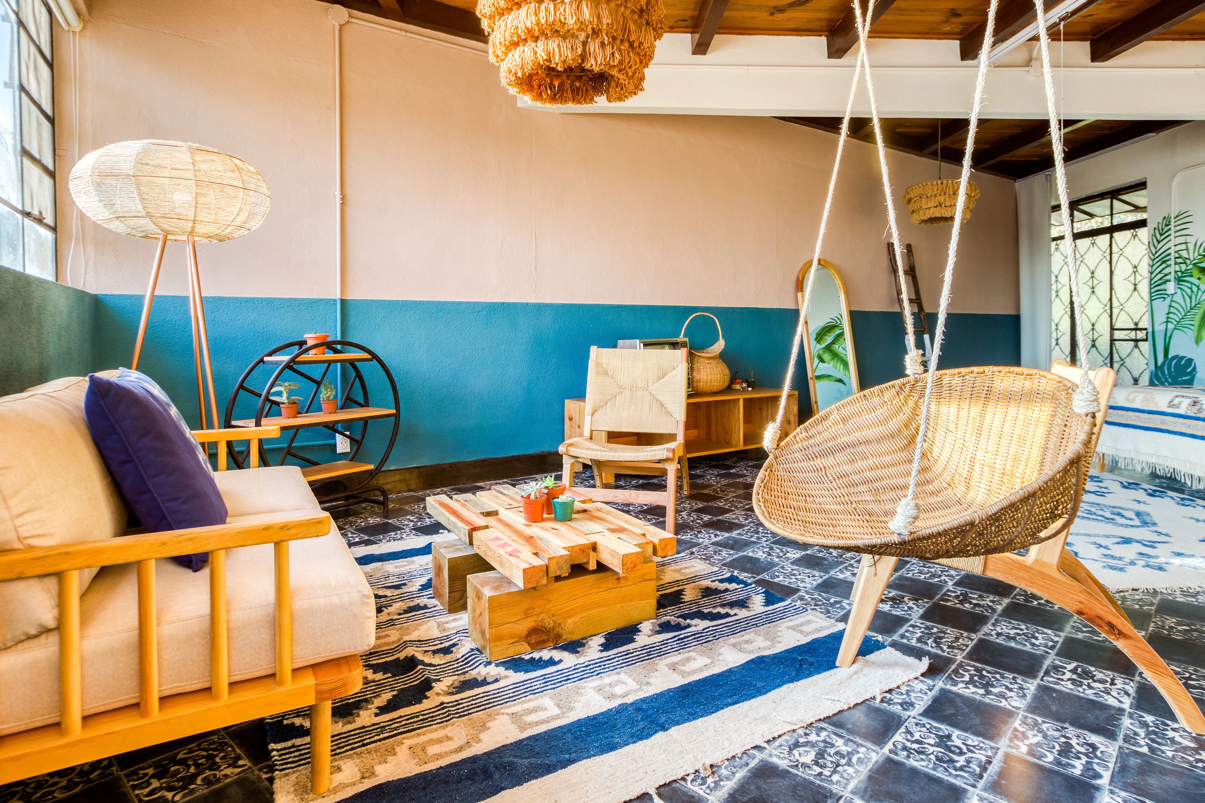 Quarto com sofá, cadeira suspensa, mesa de centro de madeira e tapete estampado.