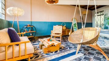 Quarto com sofá, cadeira suspensa, mesa de centro de madeira e tapete estampado.