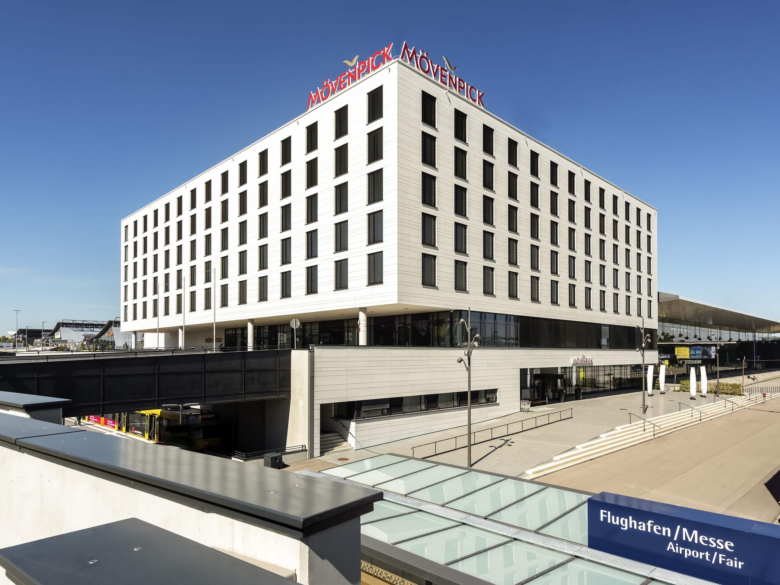 Um edifício moderno com uma grade de janelas, uma placa com a inscrição 'Mövenpick' e uma placa para 'Flughafen / Messe Airport/Fair'.