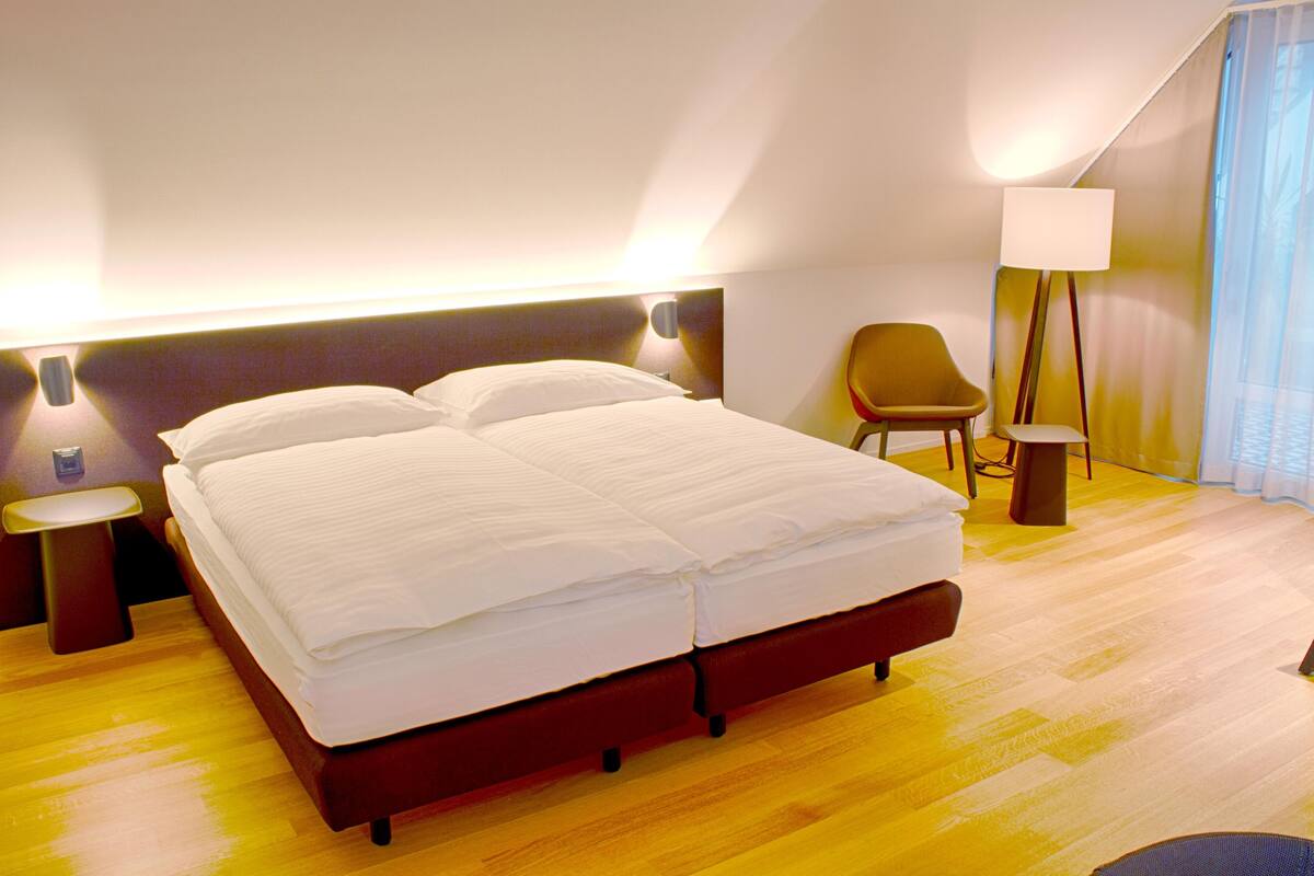 Cama bem arrumada com lençóis brancos em quarto de hotel com assoalho de madeira e cabeceira moderna.