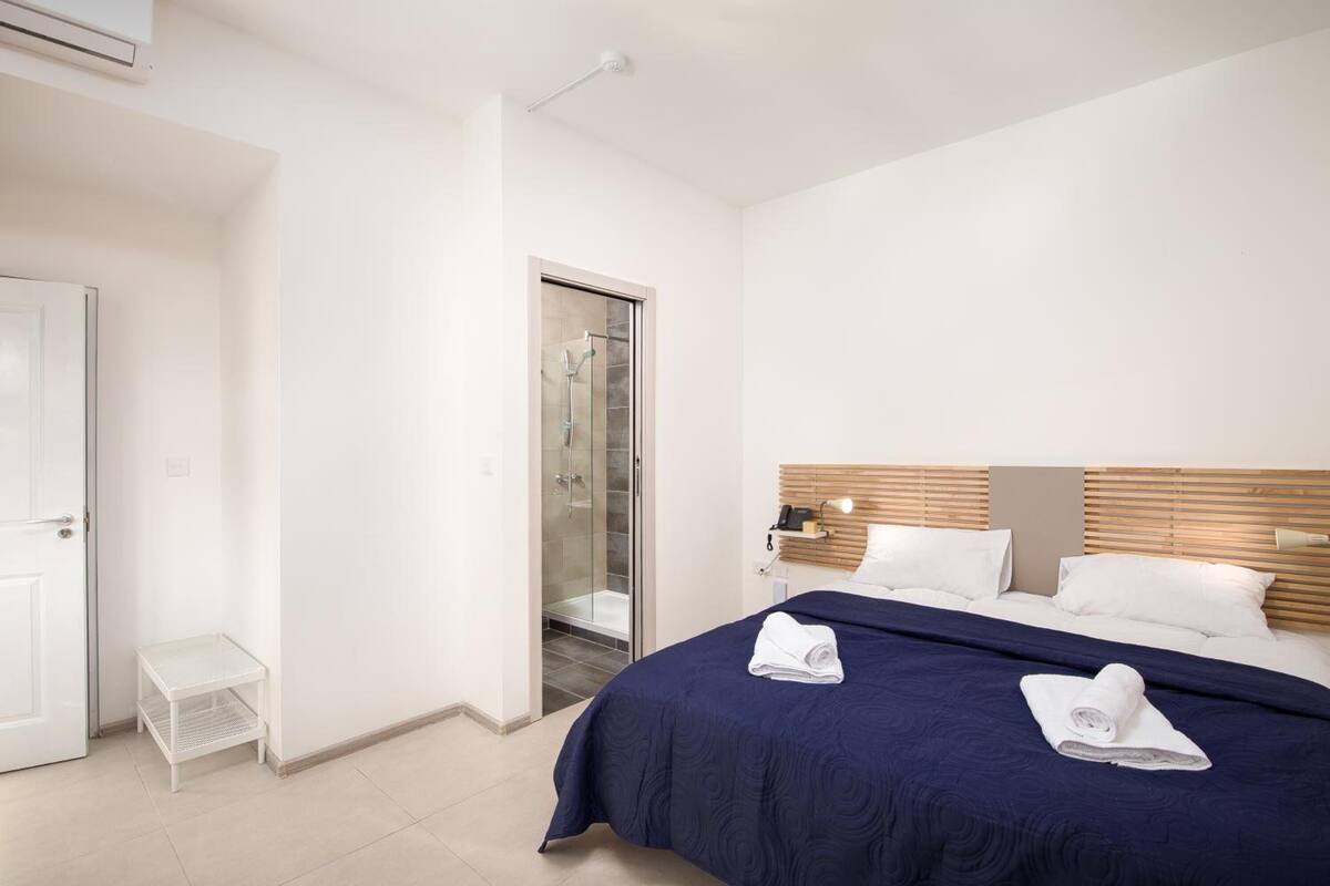 Um quarto com cama, mesa de cabeceira, chuveiro e uma porta.