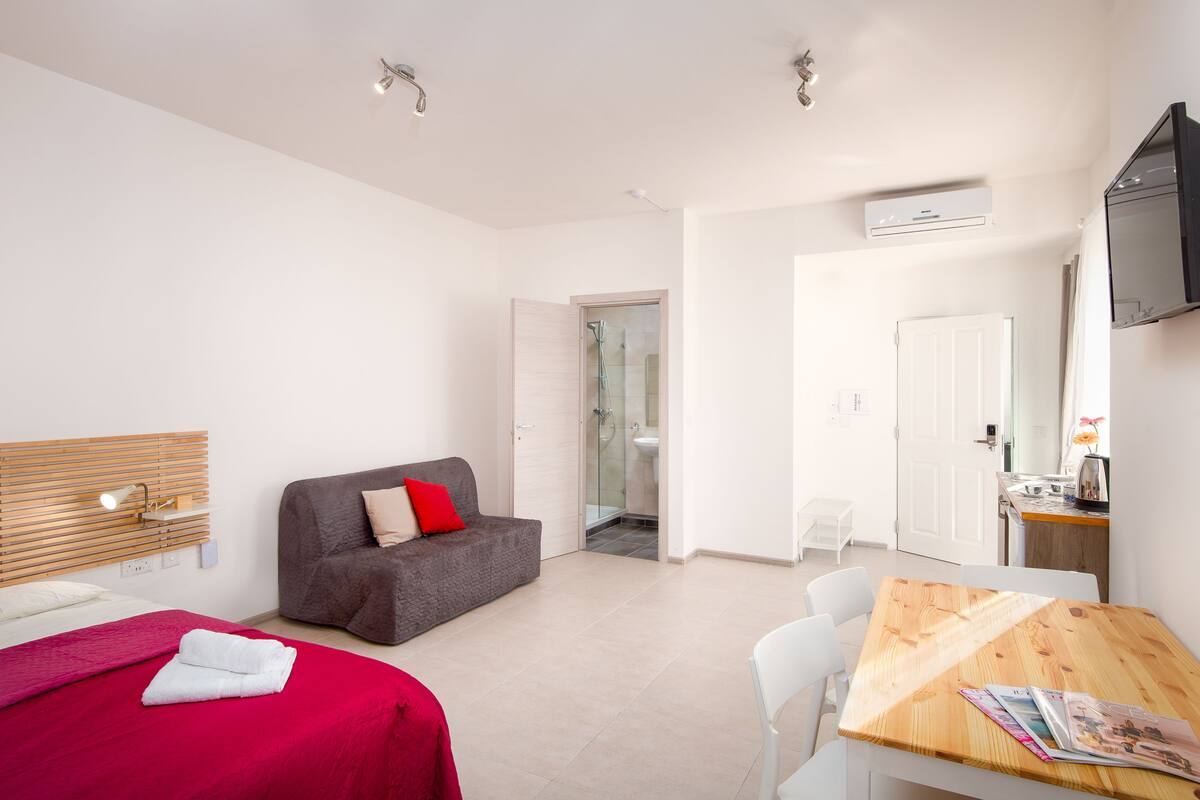 Quarto de hotel moderno com uma cama, um sofá, uma mesa de madeira e uma televisão.