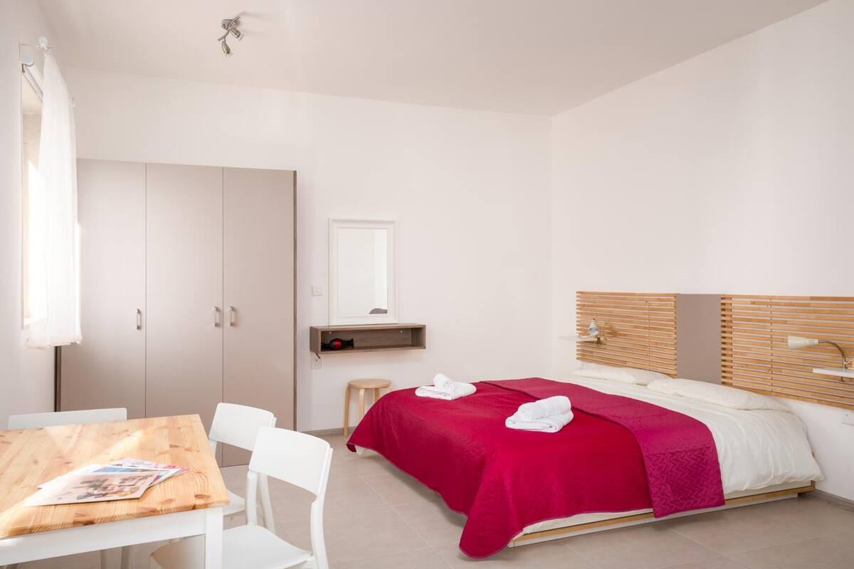 Quarto com cama, mesa de madeira, cadeira, banquinho pequeno e guarda-roupa.