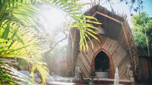 Um edifício rústico de pedra com telhado de palha, rodeado por vegetação exuberante e assentos de pedra.