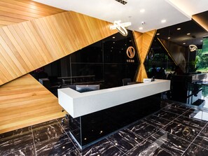 Uma receção moderna com balcão branco, soalho de mármore preto e painéis de madeira nas paredes.