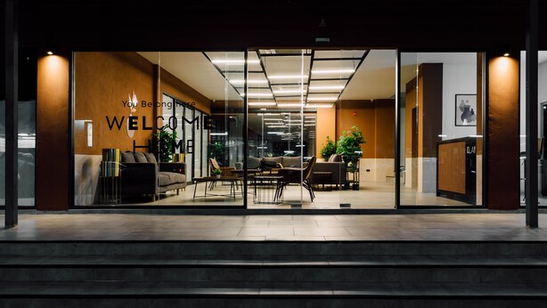 Decoração moderna com um letreiro 'WELCOME', portas de vidro e uma área de estar com sofás e cadeiras.