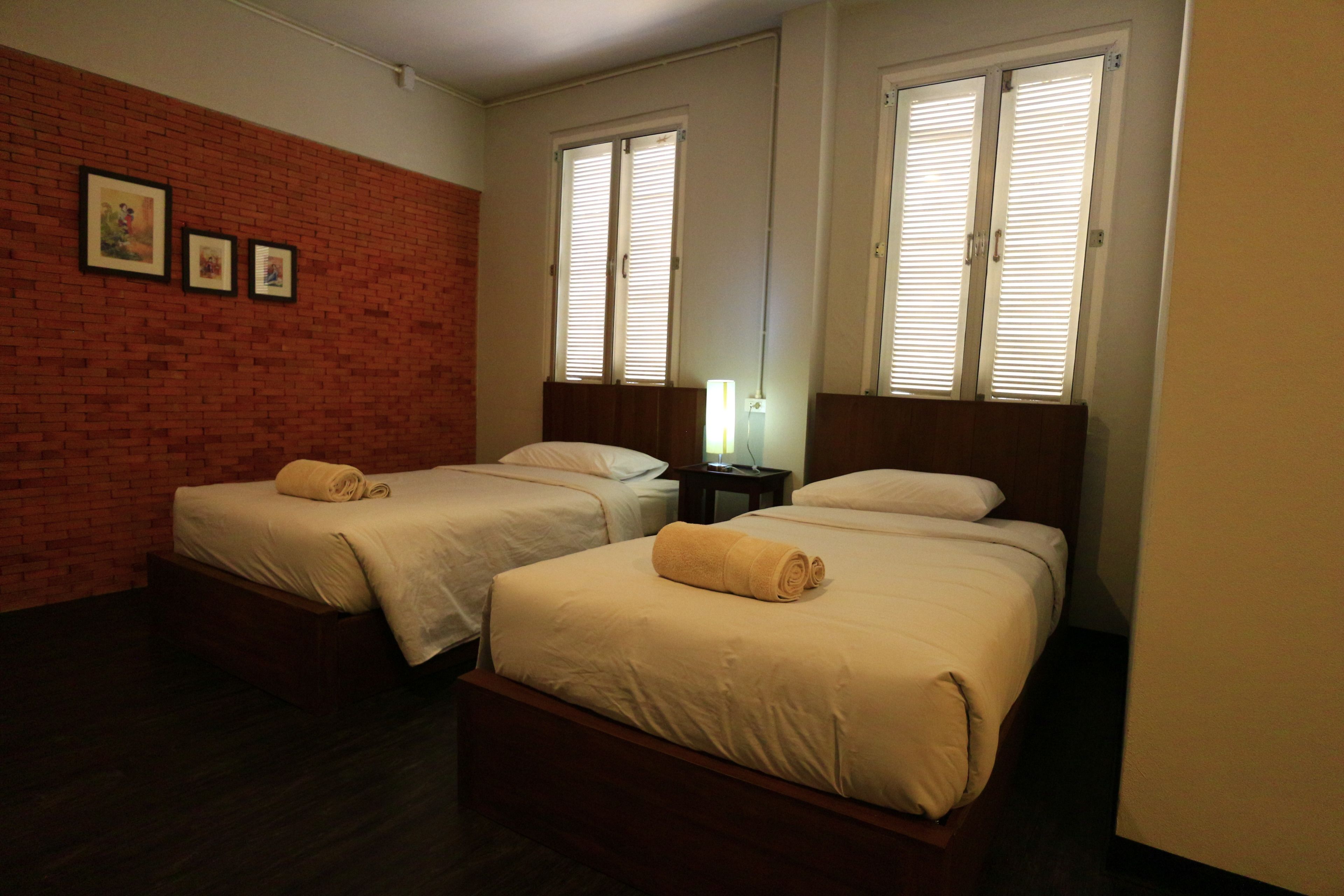 Quarto de hotel com duas camas, uma parede de tijolos e uma janela com persianas.
