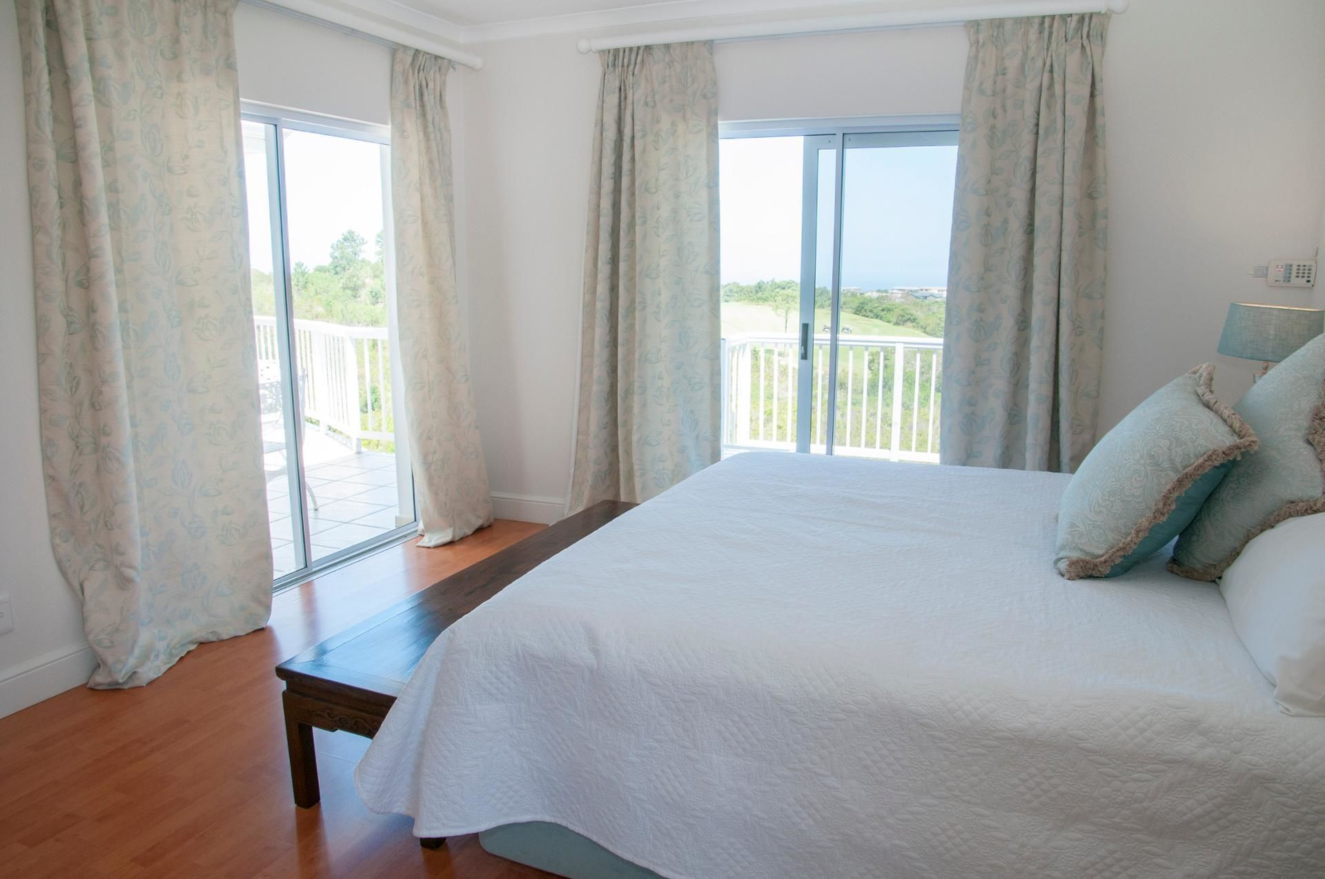 Quarto com uma cama grande, um banco de madeira e uma varanda com cortinas.