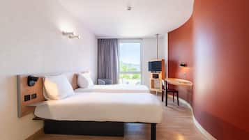 Quarto de hotel com cama, escrivaninha, cadeira, televisão e janela com vista.