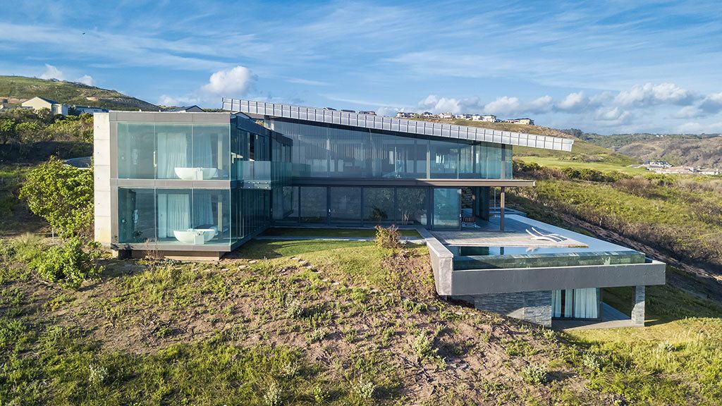Uma casa moderna com fachada de vidro, telhado plano e uma piscina grande em vidro.