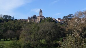 Um edifício histórico com uma torre imponente, rodeado por vegetação exuberante e árvores.