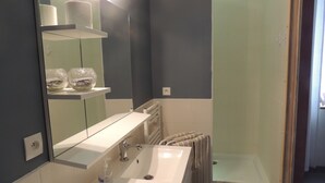 Um banheiro moderno com pia branca, um espelho grande e box de vidro.