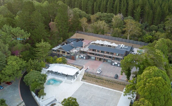 Vista aérea de um hotel com piscina, vários edifícios e uma floresta ao redor.