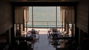 Quarto com vista para o oceano, com área de jantar e mesas, janelas amplas com cortinas e escada que leva a uma área externa.