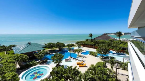 Um resort com uma grande área de piscina, vista para a praia e um pavilhão coberto.