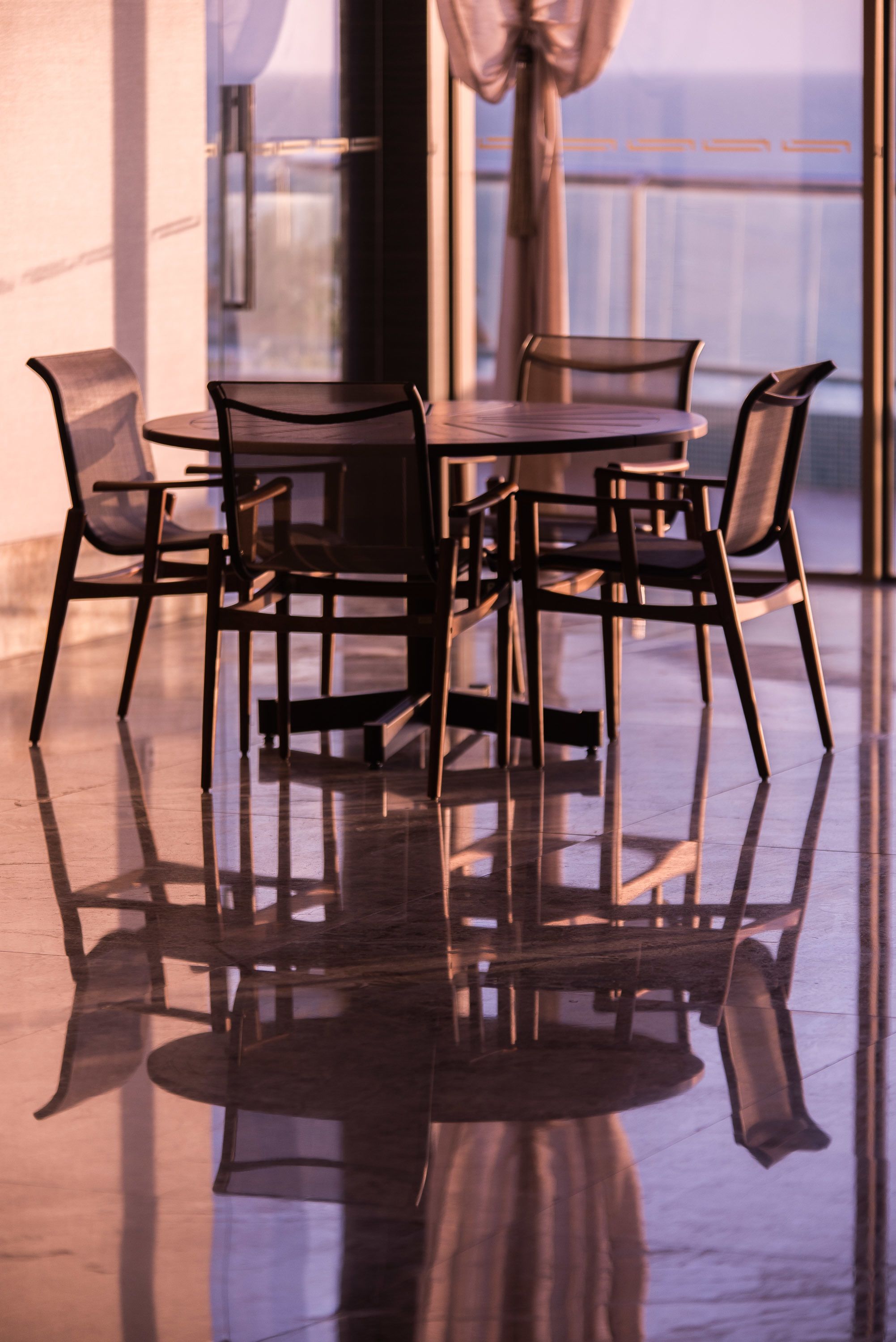 Uma área de refeições com uma mesa redonda e quatro cadeiras, uma divisória de vidro e vista para o exterior.