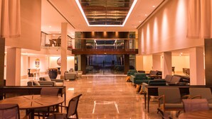 Um hall espaçoso com teto alto, mobiliário moderno e vista do céu através de uma parede de vidro.
