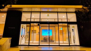 Entrada de hotel com fachada moderna, letreiros iluminados e porta de vidro.