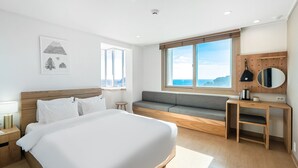 Quarto de hotel moderno com uma cama grande, área de estar, escrivaninha de madeira e uma janela ampla com vista.