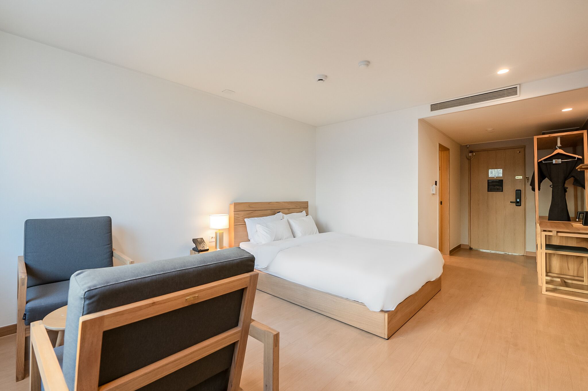 Quarto de hotel moderno com uma cama grande, área de estar com uma cadeira e mesa, guarda-roupa e espelho.