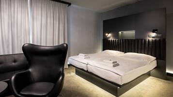 Quarto de hotel moderno com uma cama grande, uma poltrona de couro preto e um aplique na parede.