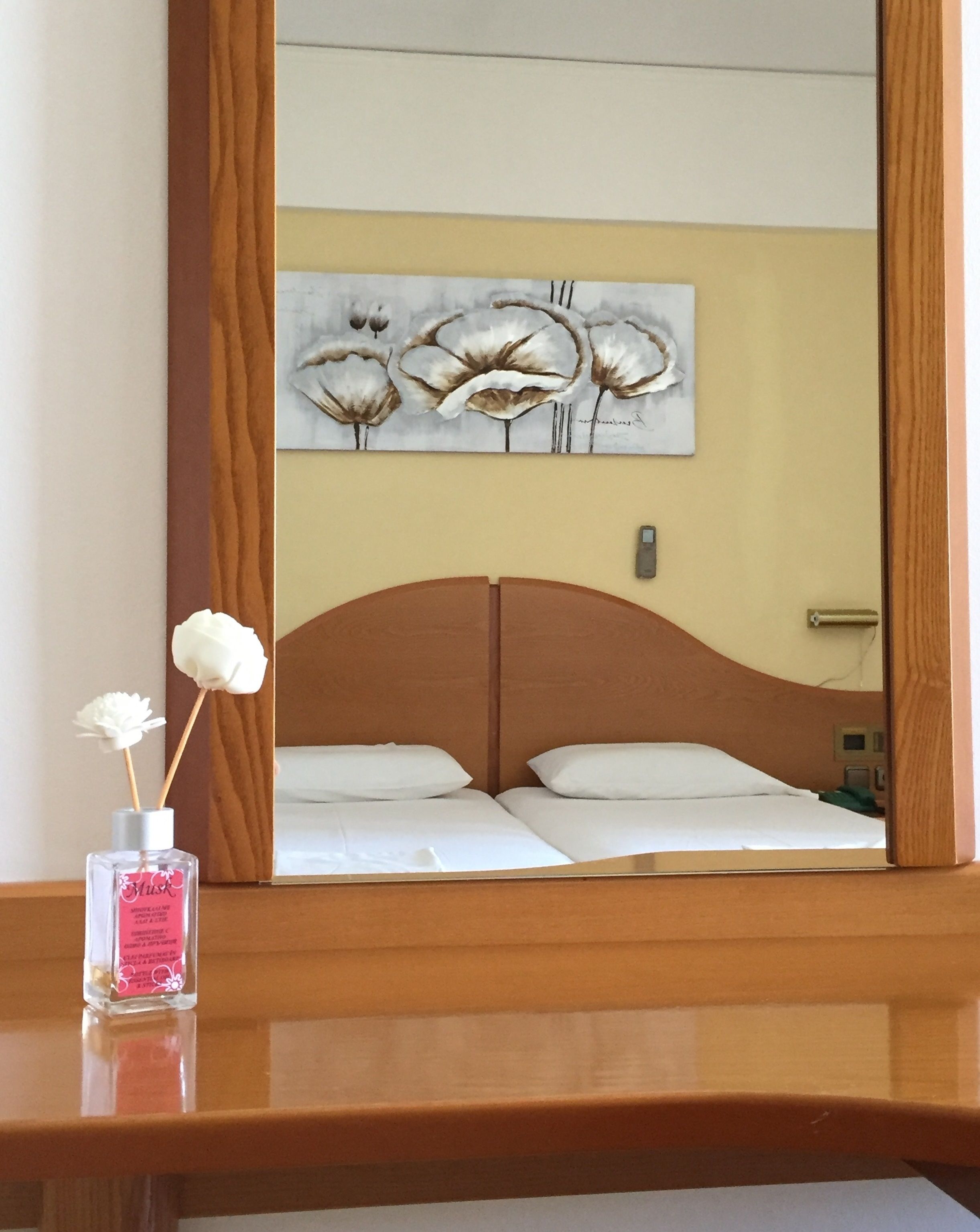 Quarto de hotel com cabeceira de madeira, cama com roupa de cama branca, vaso com flores e um quadro na parede.