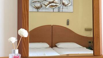 Quarto de hotel com cabeceira de madeira, cama com roupa de cama branca, vaso com flores e um quadro na parede.