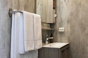 Casa de banho com porta-toalhas, lavatório, espelho e prateleira com garrafa e copos.