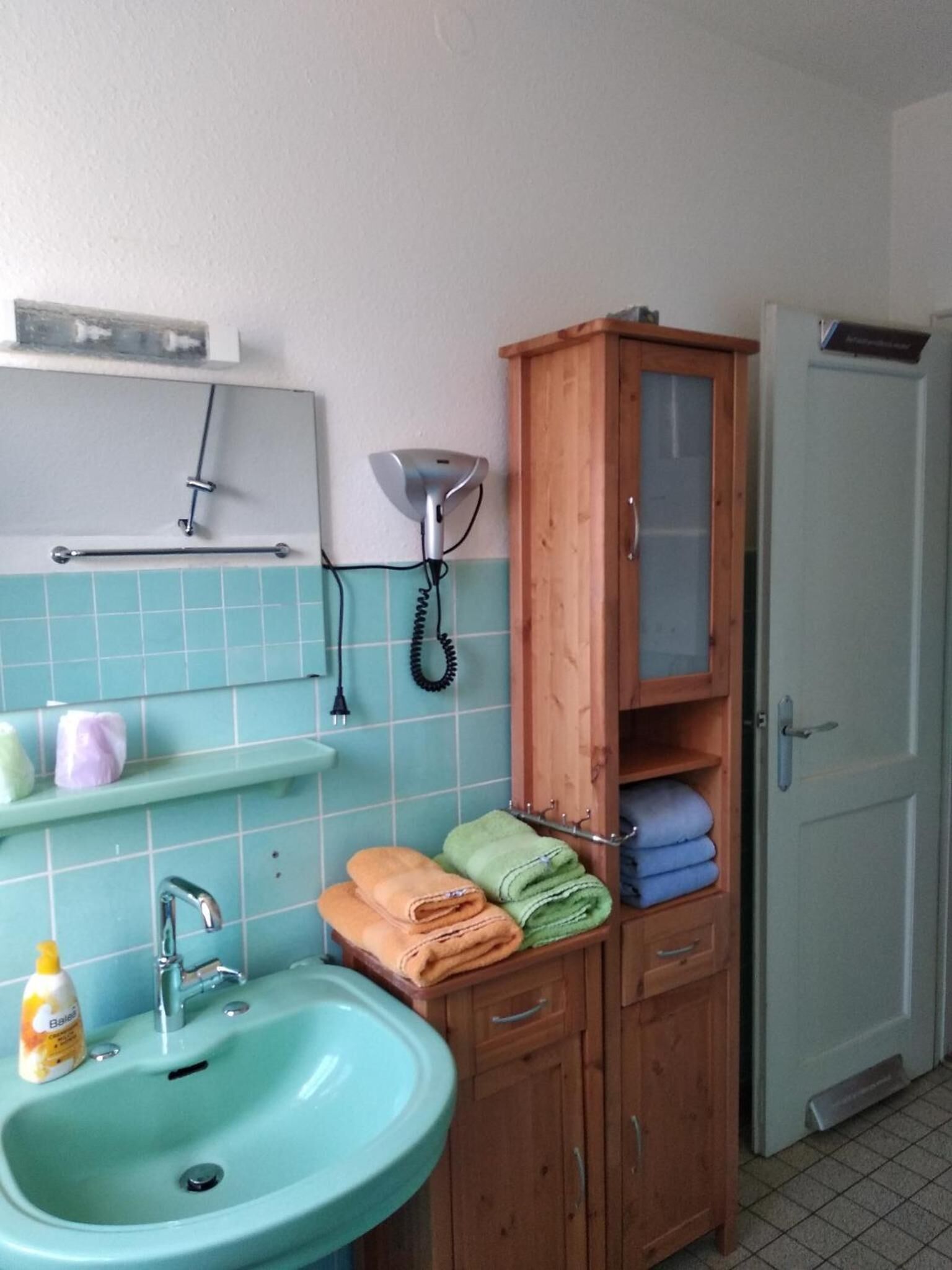 Uma casa de banho com uma pia, um armário de madeira com portas de vidro e um porta-toalhas com toalhas dobradas.