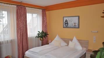 Quarto de hotel com cama, cortinas, quadro na parede, abajur e mesa de cabeceira.